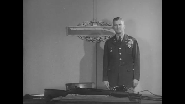 1940s: Officer sits behind desk with combat rifle on top and speaks ...