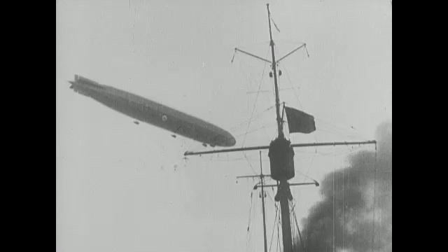 1910s: Zeppelin flies over burning ship. Submarine. Men stand. Burning ...