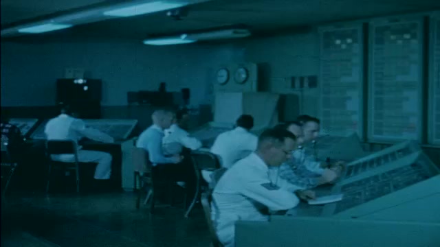 1960s: Dimly lit control room with men in white military coveralls at ...