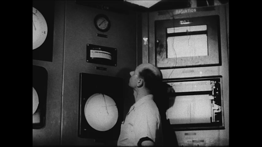 1950s: Control room of nuclear reactor. Man checks gauge. Man turns ...