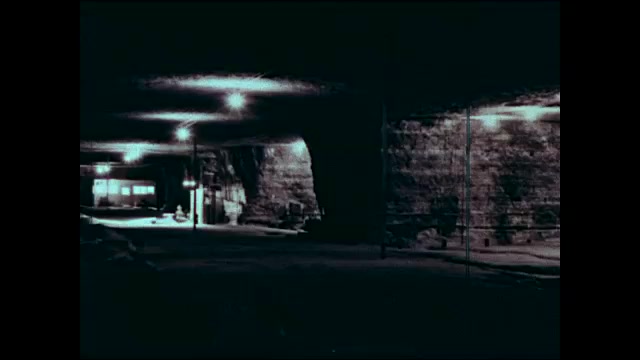 1960s: Lights line ceiling of salt mines. Man adjusts controls on ...