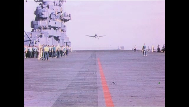 1940s: Aircraft carrier from the air. Airplane lands on the carrier ...