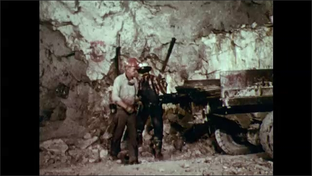 1970s: Two men walk through mine tunnel. Two men pull beams from back ...