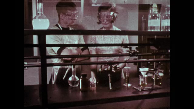 1960s: Students work at laboratory table. Boy and girl look at each ...