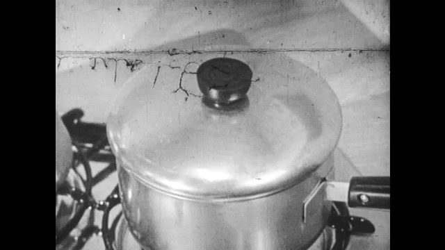 1950s: UNITED STATES: hand lifts lid of pot on stove. Food cooks in pan ...