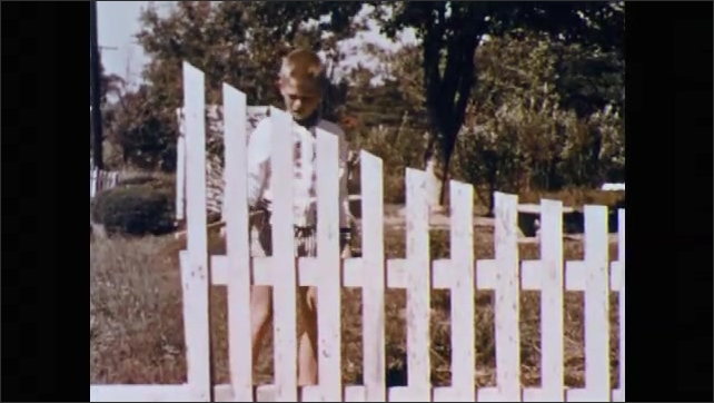 1950s: Boy hits fence with stick, looks at stick. Boy runs stick across ...