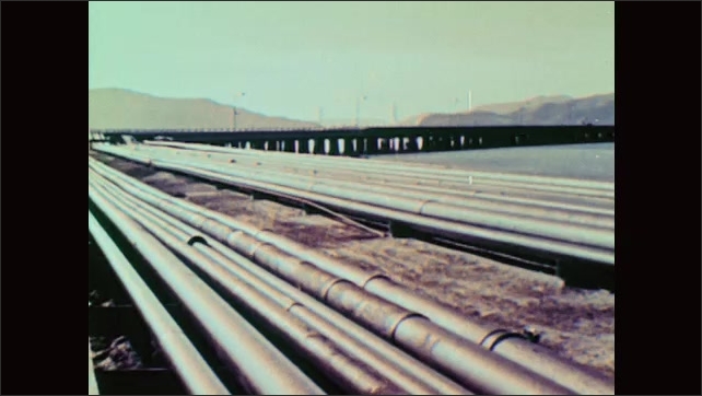 1950s: Oil strorage tanks next to shore. Pan across pipeline by wharf ...