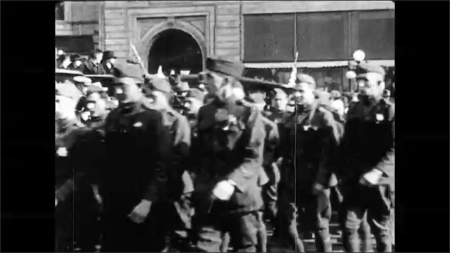1920s: Under a Welcome Home sign, a large crowd marches down street ...