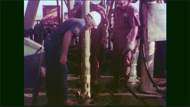 1970s: Drill pipe and coupling lowers through the hole in the oil rig ...