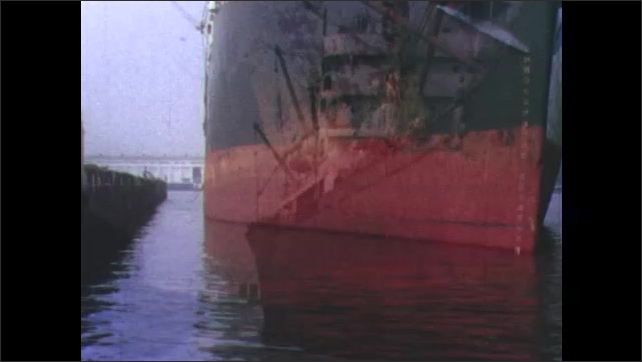 1950s: cargo ship with loading arms sits in the water next to dock as ...