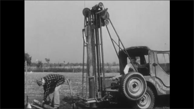 1960s: UNITED STATES: farmer digs post hole in ground. Man with machine ...
